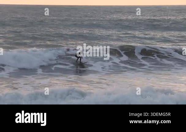 Surfer in warm wetsuit riding wave on board at sunset. Winter sports in ...