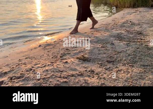 Womans feet walking along the shoreline with golden sunlight reflecting ...
