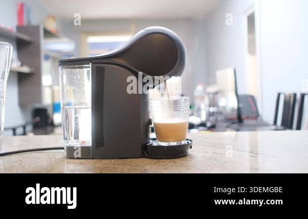 Capsule coffee machine brewing fresh espresso into a glass cup on a ...