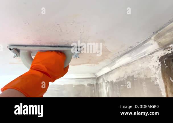 Close-up of a workers hand in an orange glove sanding a ceiling with a ...