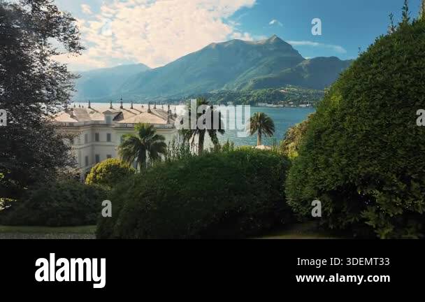 View through palm and greenery at Lake Como with elegant white building ...
