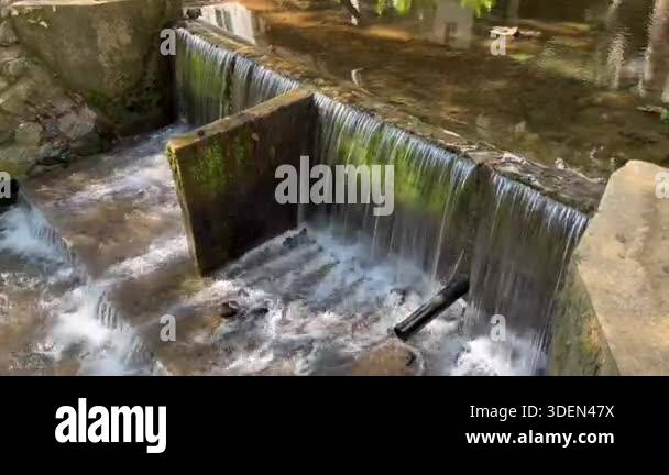 Flowing water over a small concrete weir in rural river, showing water ...