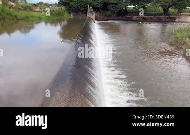 Flowing water over a small concrete weir in rural river, showing water ...
