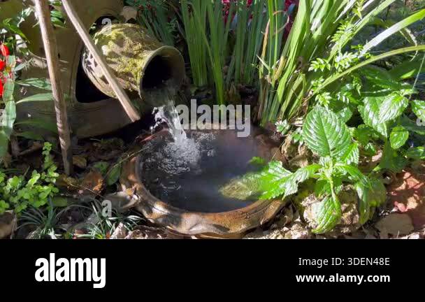 Water flowing from an old clay pot into a small basin surrounded by ...