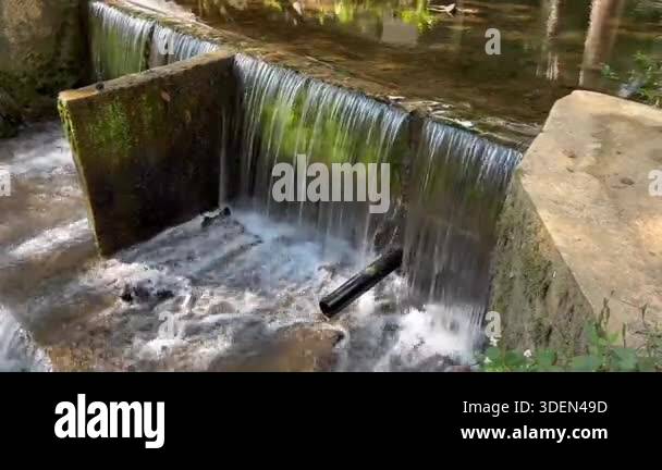 Flowing water over a small concrete weir in rural river, showing water ...