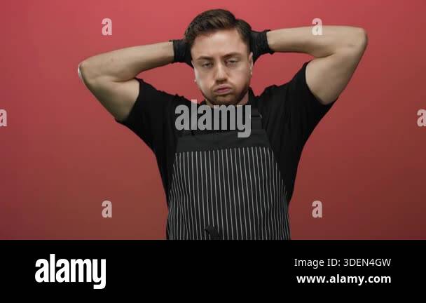 Young man with beard wearing apron and gloves stands against isolated ...