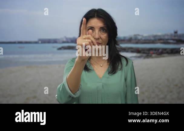Woman pointing finger to camera at sandy beach shore with distant ocean ...