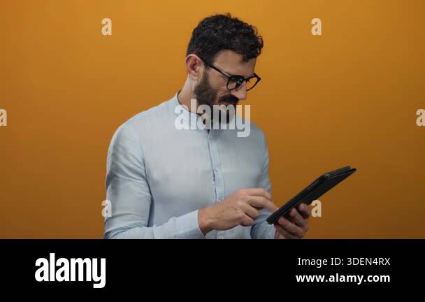 Hispanic man with beard holds a tablet against a vibrant orange ...