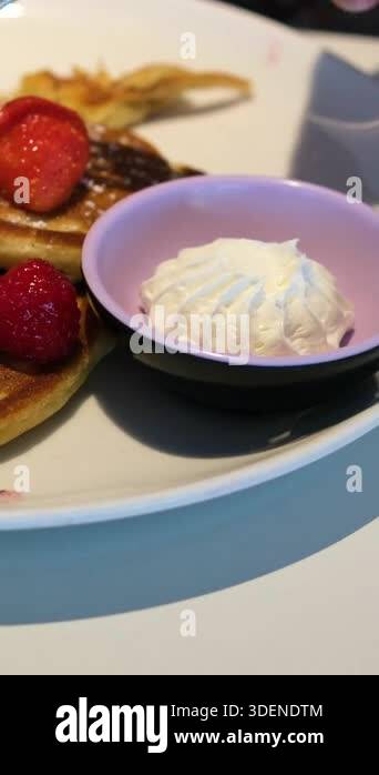 pancake stack topped with cream, berries, and syrup, served on a dark ...