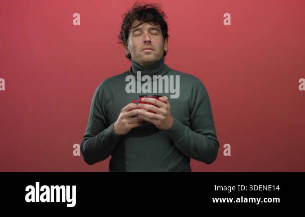 Hispanic man enjoys coffee with a serene expression against a red ...