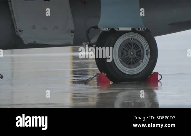 Military aircraft landing gear wheel secured with chocks on wet runway ...