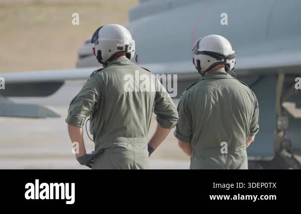 Rear view of two pilots in flight gear observing a fighter aircraft ...