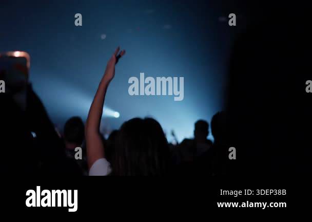 Silhouetted arm extends upward amid dense crowd bathed in blue ...