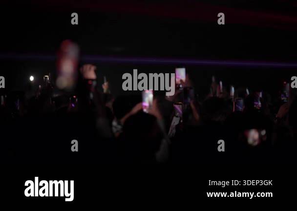 Crowd filming concert performance with raised smartphones and bright ...