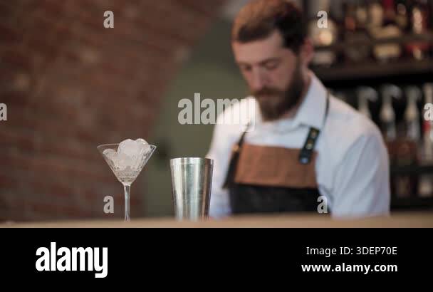 A barman prepares a cocktail in a bar. He adds ice to a shaker ...
