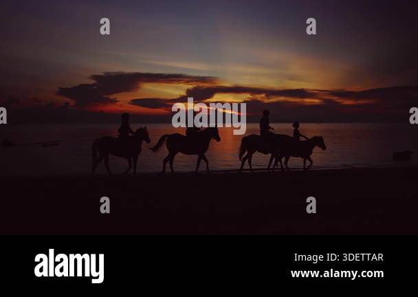 Silhouettes of Horse Riders Moving Along Beach at Sunset with Fiery Sky ...