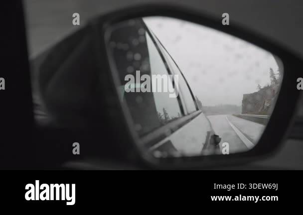 Reflection of receding wet asphalt road in car side wing mirror. View ...