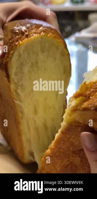 A closeup of hands tearing a freshly baked loaf of bread, showing its ...