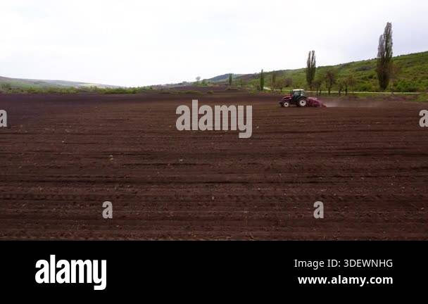 A red tractor engages in plowing a vast field, turning over soil and ...