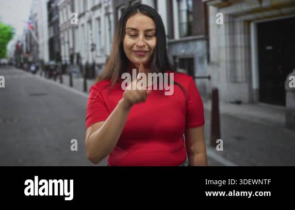 Woman finger to lips covering mouth on street wearing red shirt near ...