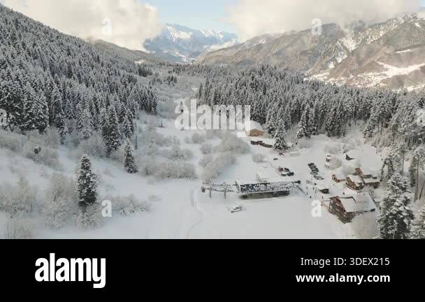 Aerial static snow covered pine forest and wooden hut near ski resort ...