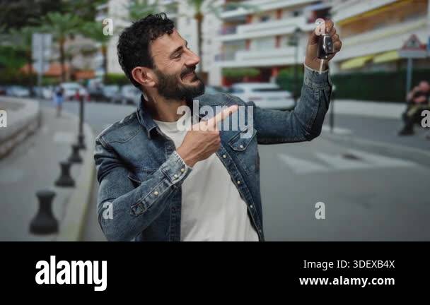 Hispanic man with beard holding car keys on a vibrant outdoor street ...
