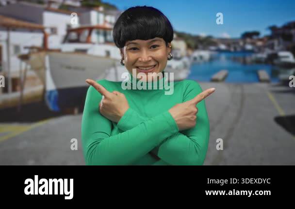 Chinese woman points in opposite directions smiling at a seaside port ...