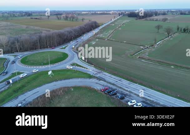 Cars navigate a multi-lane roundabout with surrounding roads and fields ...
