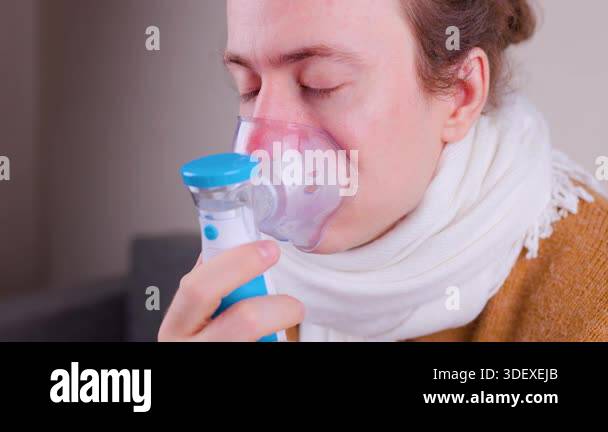 Man with red nose and scarf using a portable nebulizer inhaler at home ...