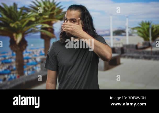 Man with hand covering face on beach street promenade near palm trees ...