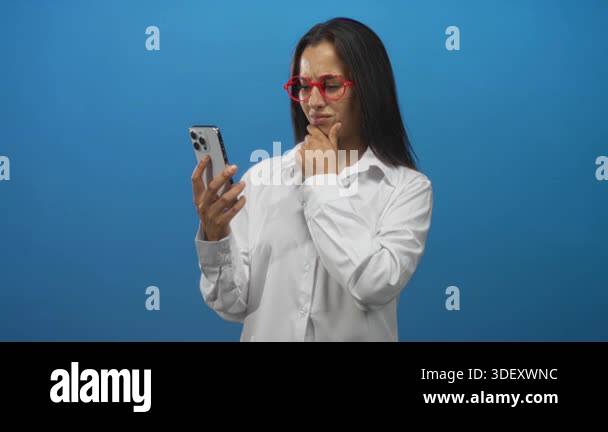 Woman holding smartphone with hand on chin showing pensive pose in blue ...