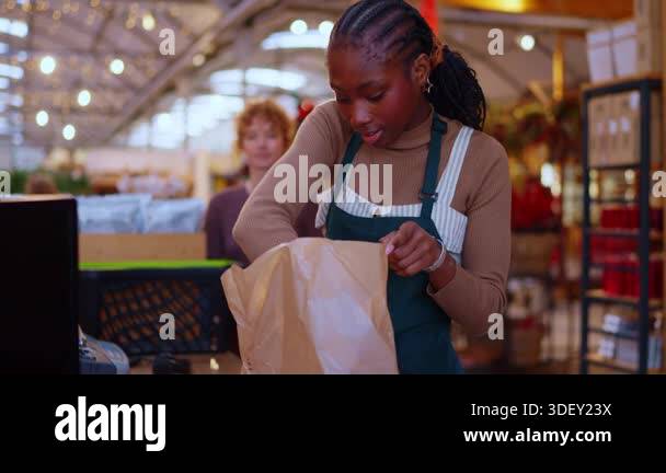 Young female grocery clerk at the checkout counter carefully placing ...