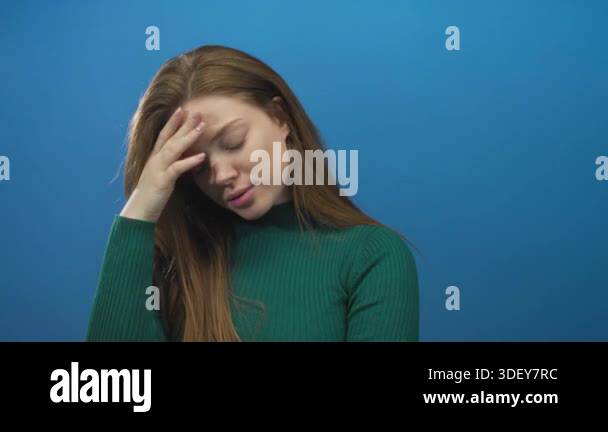 Woman with long red hair wearing green sweater with hand on forehead ...