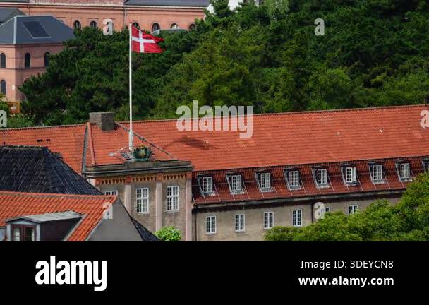 Danish flag waving on a flagpole above a building with a red tiled roof ...