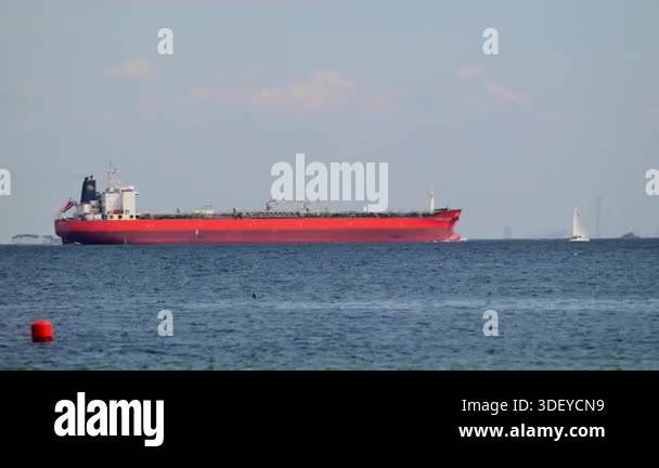 Oil tanker sailing on sea, transporting cargo with a sailboat in the ...