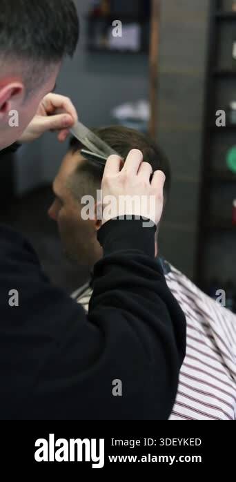 A young male Barber adjusts the hair of a male client. Professional ...