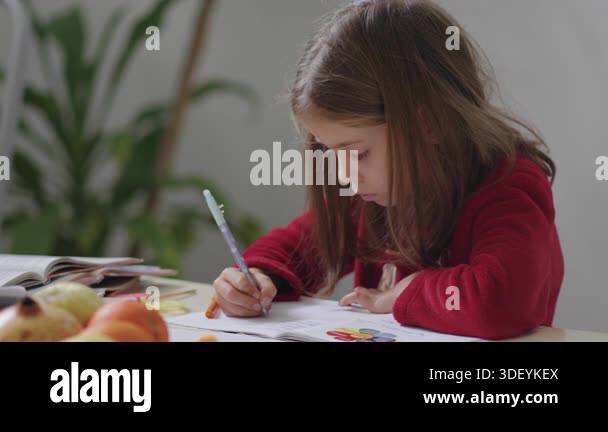 Pretty girl in red pajamas doing homework at table in kitchen at home ...