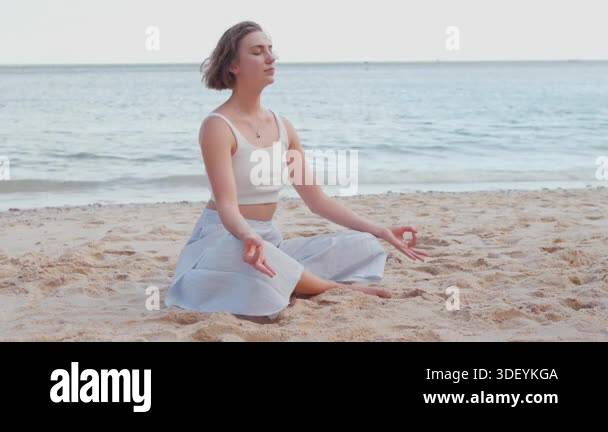 Woman practicing Lotus Pose on sandy beach near ocean with hands in ...