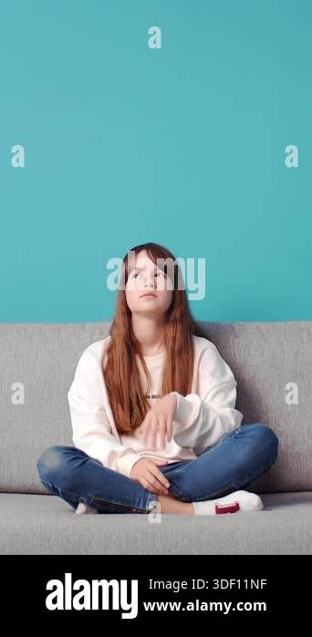 A girl sits on a couch with a blue wall in the background thinking of ...