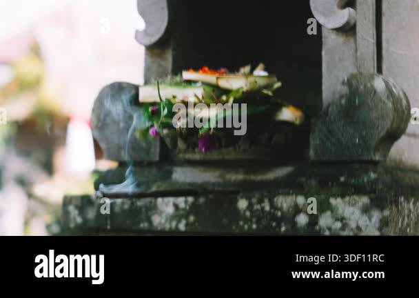 Traditional Balinese offering on a stone shrine with incense smoke; a ...
