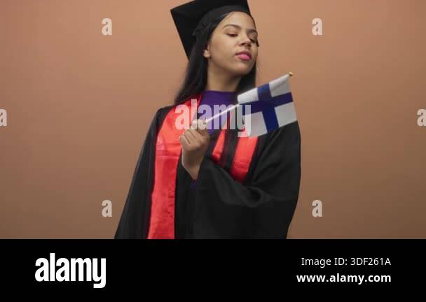 Young woman in graduation gown smiles while waving finland flag with ...