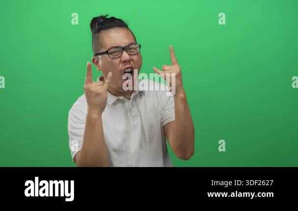 Man shouting with rock horns gesture in green studio, hands raised and ...