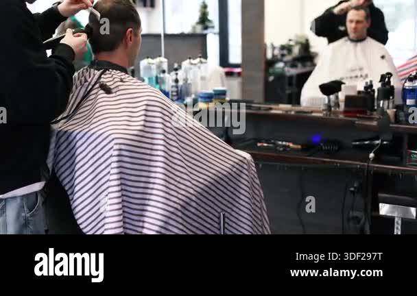 A young male Barber adjusts the hair of a male client. Professional ...