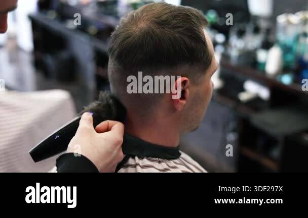 A young male Barber adjusts the hair of a male client. Professional ...