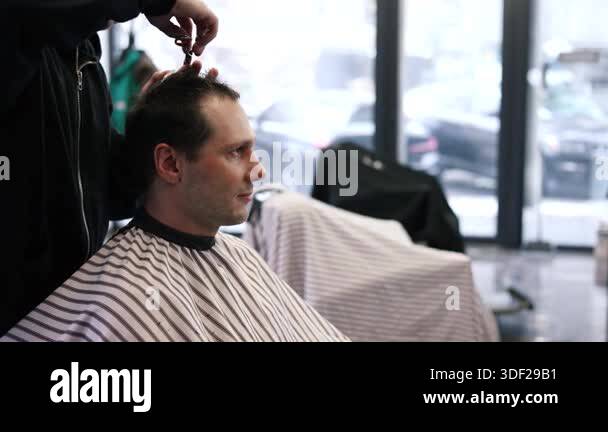 A young male Barber adjusts the hair of a male client. Professional ...
