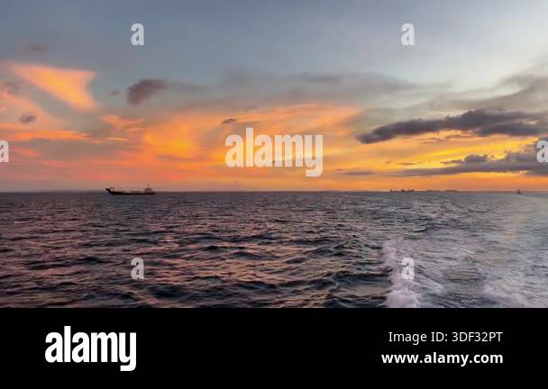Peaceful ocean sunset with vibrant orange and yellow skies, boat wake ...