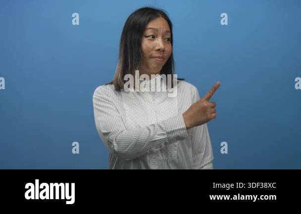 Woman points finger to the right in blue studio while crossing her ...