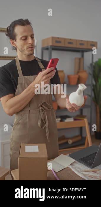 Man in studio holding white ceramic vase and checking red smartphone ...