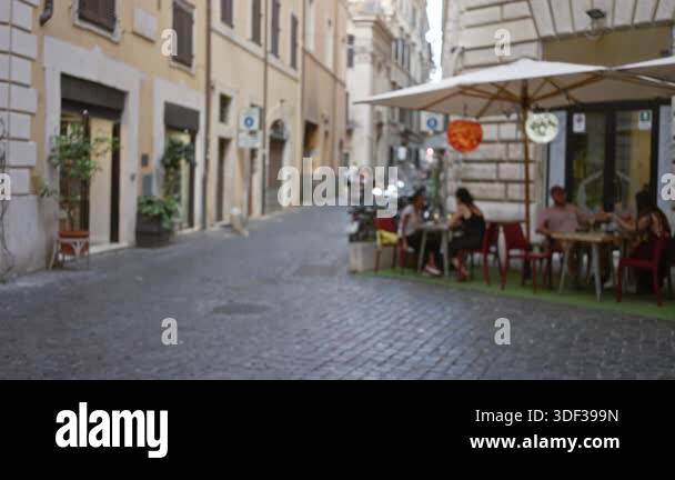 Rome narrow cafe terrace with umbrellas and cobblestone, softly blurred ...