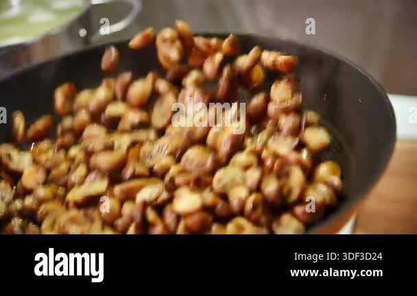 Close-up slow motion of small golden button mushrooms being fried in a ...